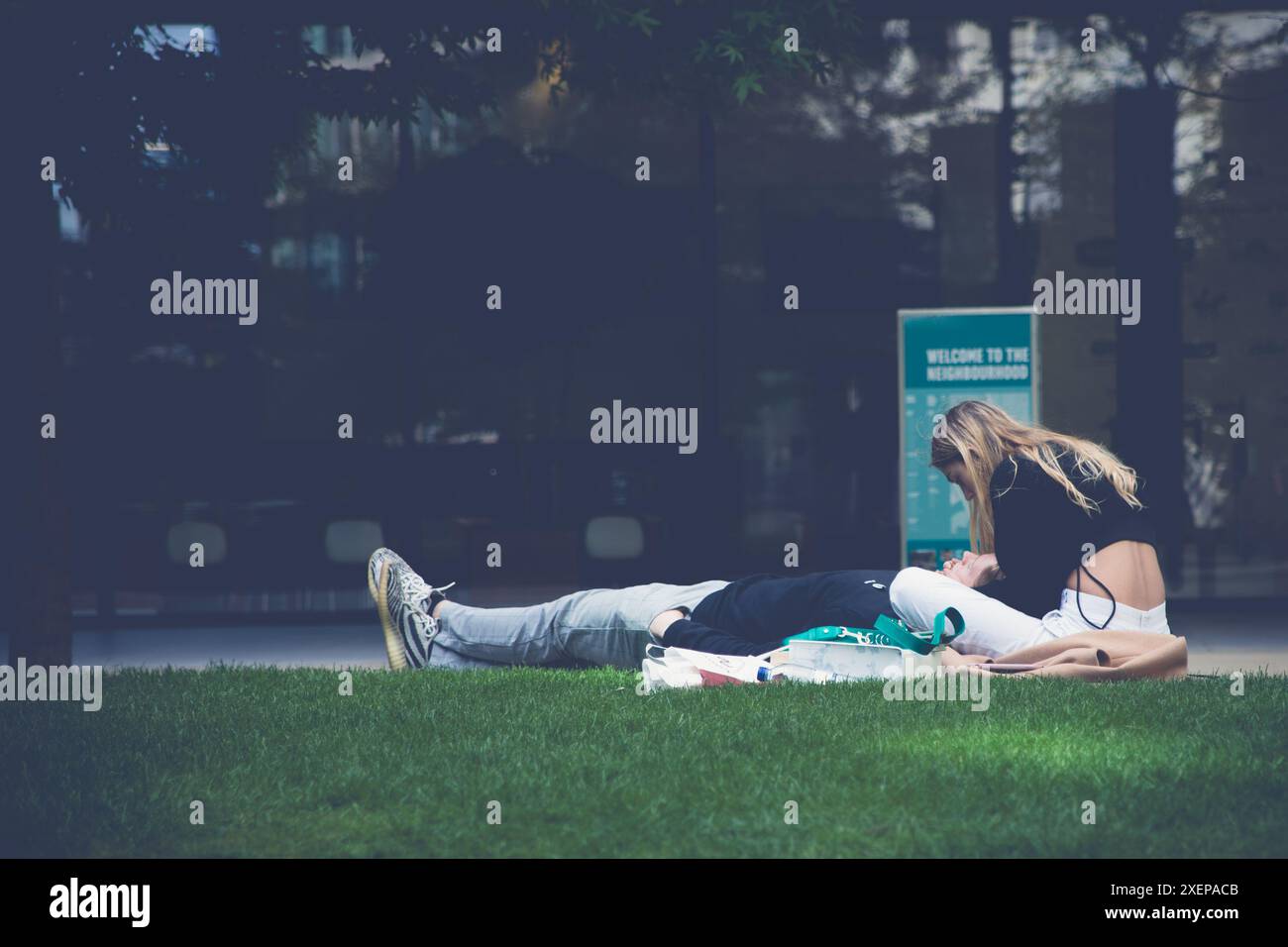 A woman sits on some grass with her partner lying down with his head ...