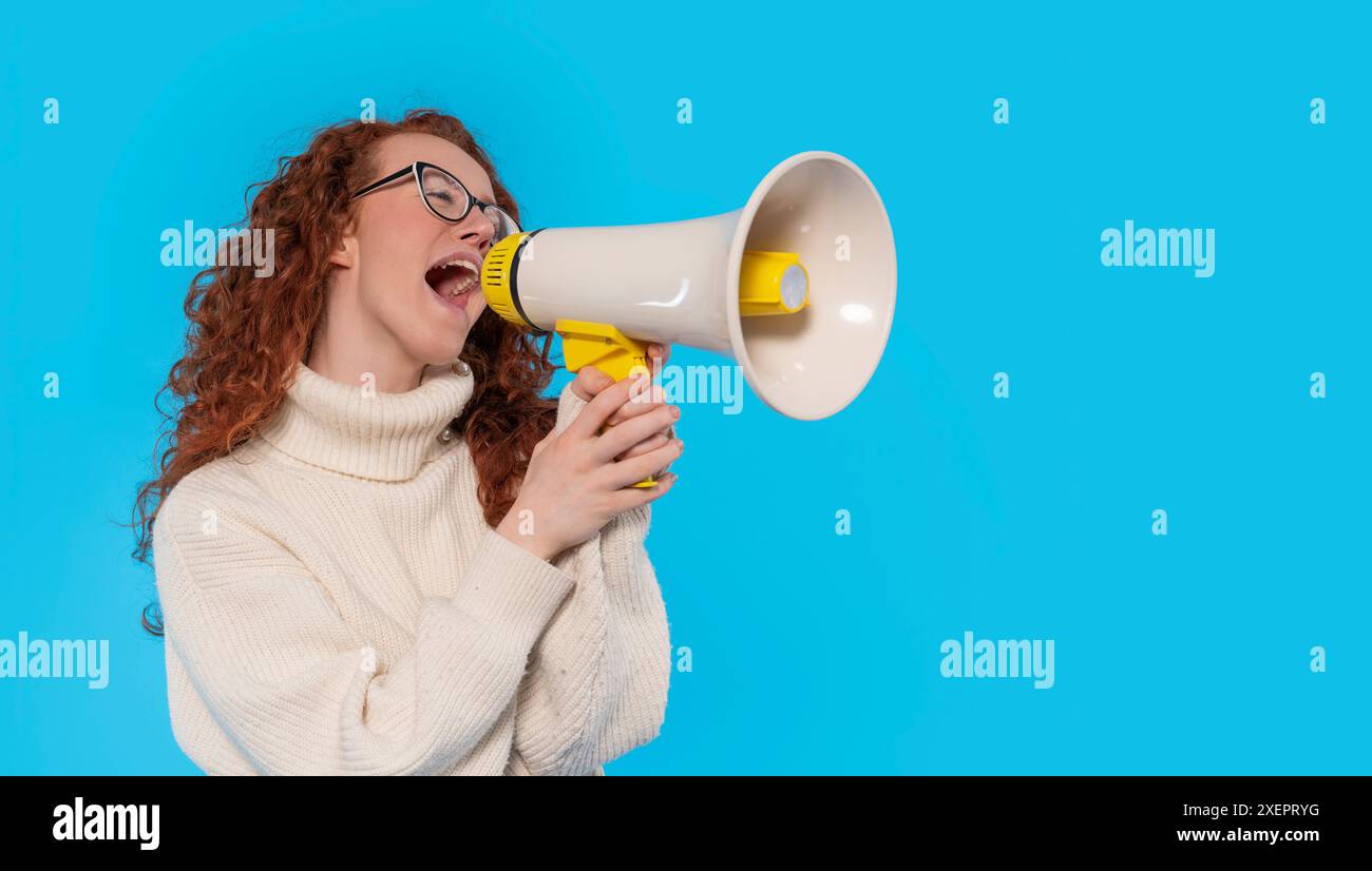 Redhead woman in white sweater making an announcement with a megaphone ...