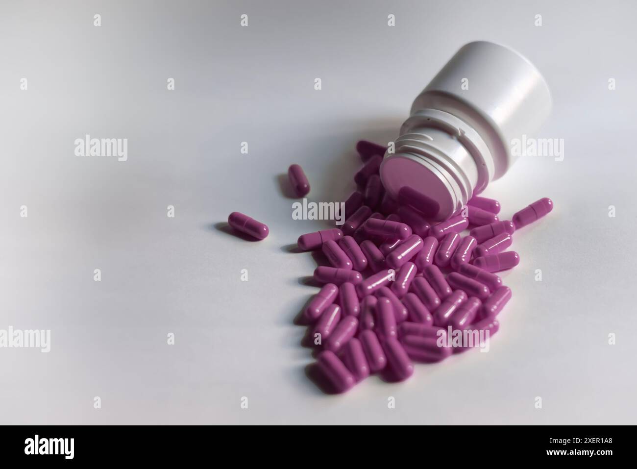 Pink pills scattered outside a white medicine bottle, representing ...