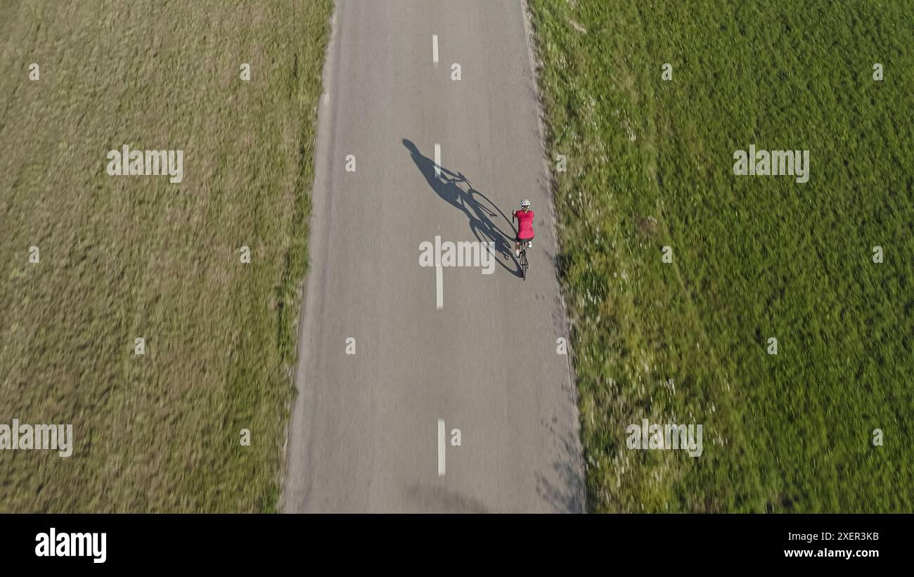 Rear view of a female racing cyclist riding on an empty asphalt road ...