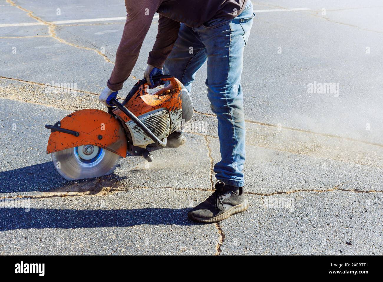 Construction worker cuts damaged asphalt in parking with diamond blade ...