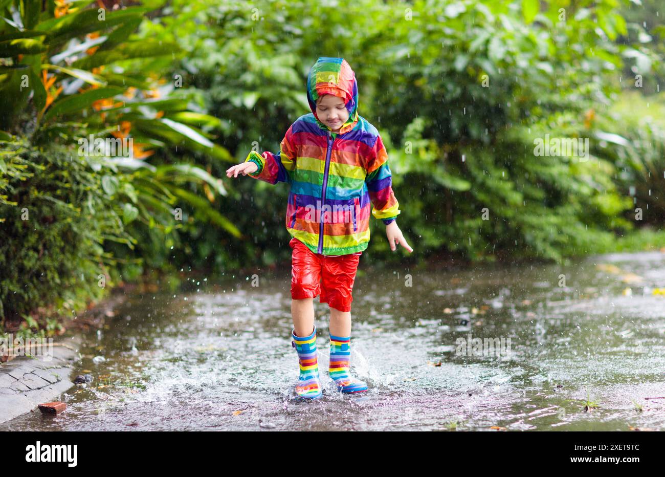 Kid playing in the rain in autumn park. Child jumping in muddy puddle ...