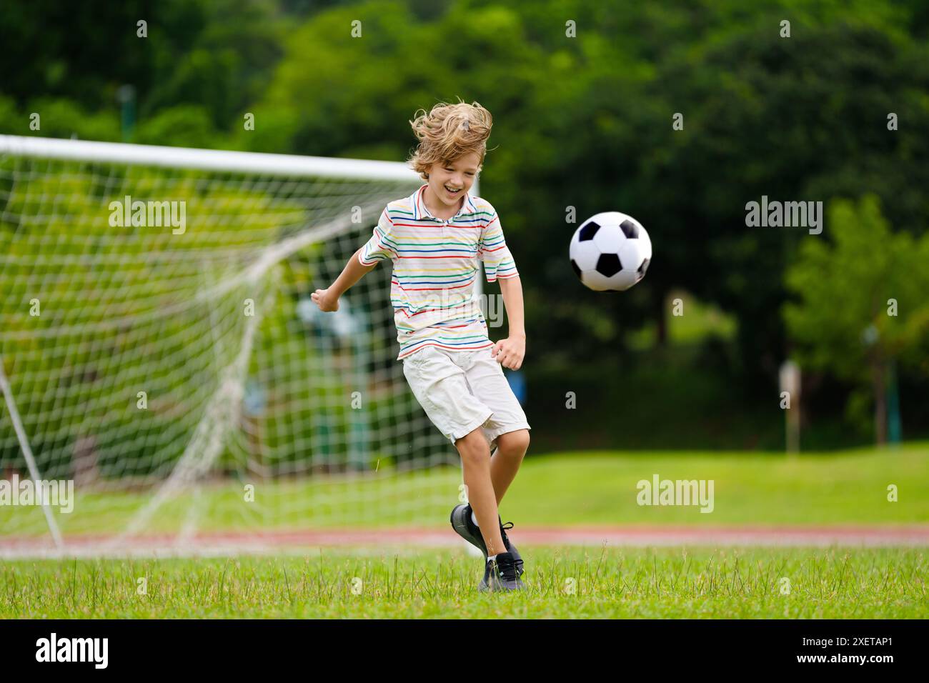 Child playing football. Kids play soccer on outdoor pitch. Little boy kicking ball in summer ...