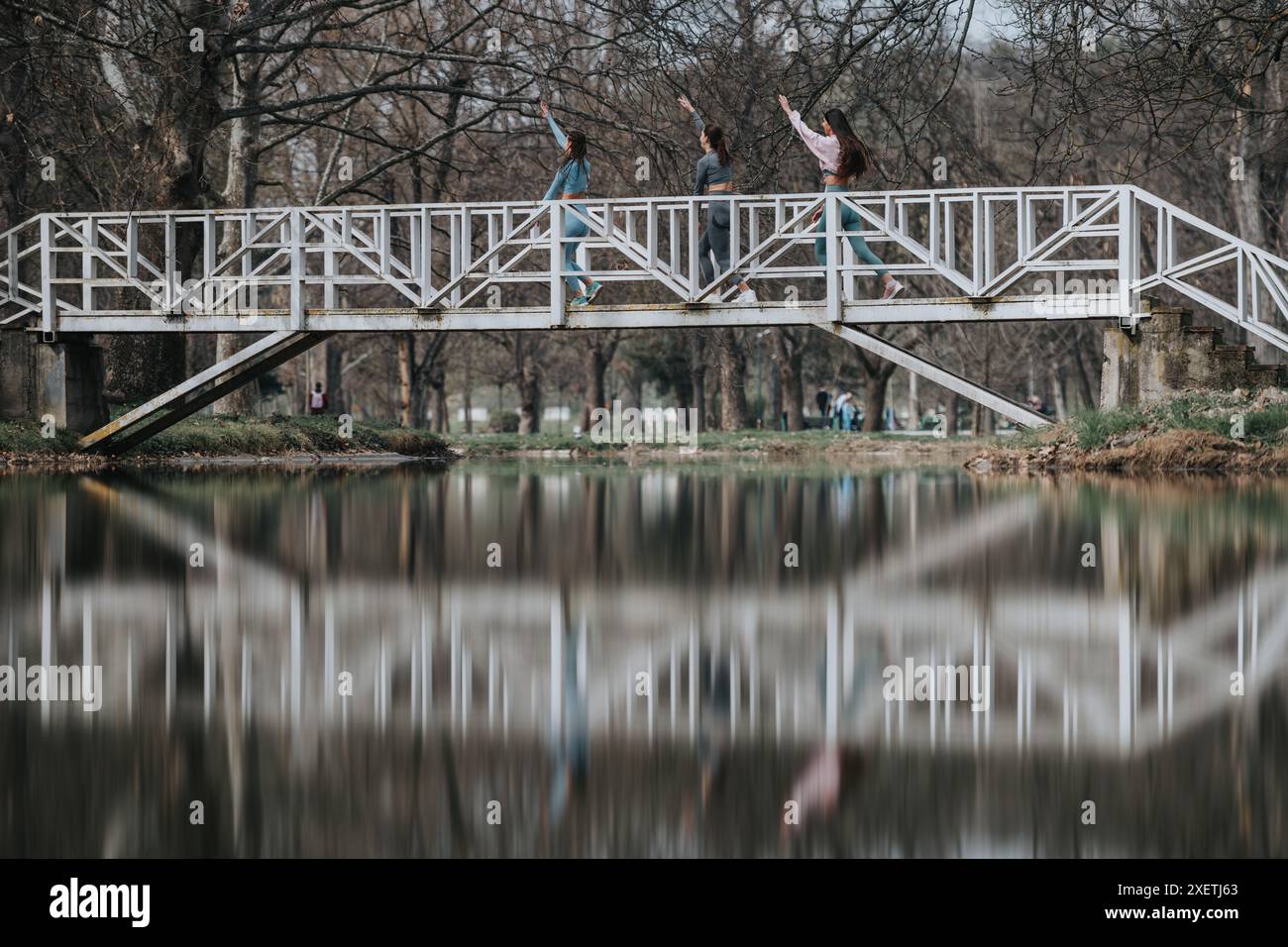 Female athletes jogging and stretching on a bridge over a tranquil ...
