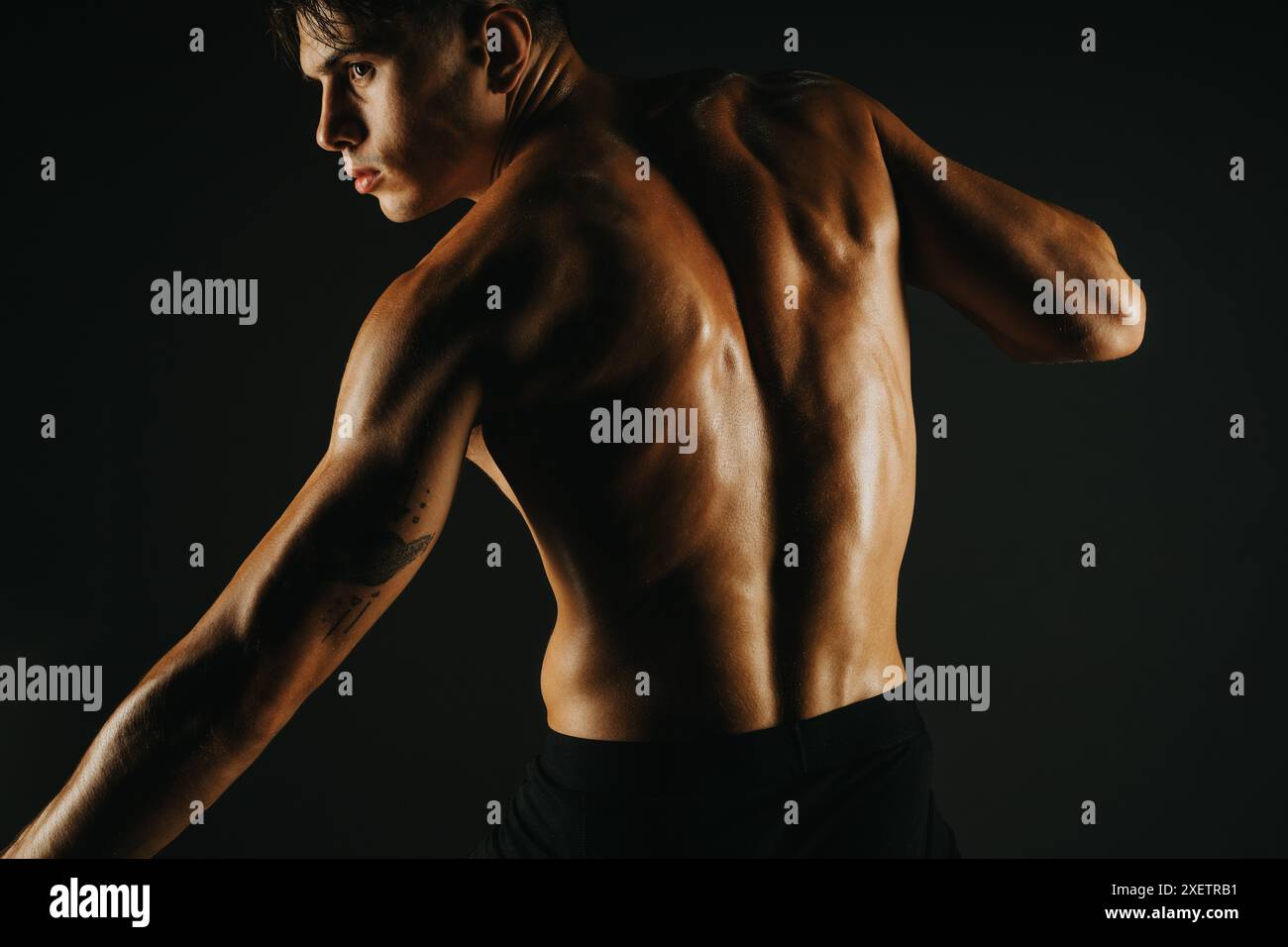 Fit man showing his back muscles in a dark setting highlighting his ...