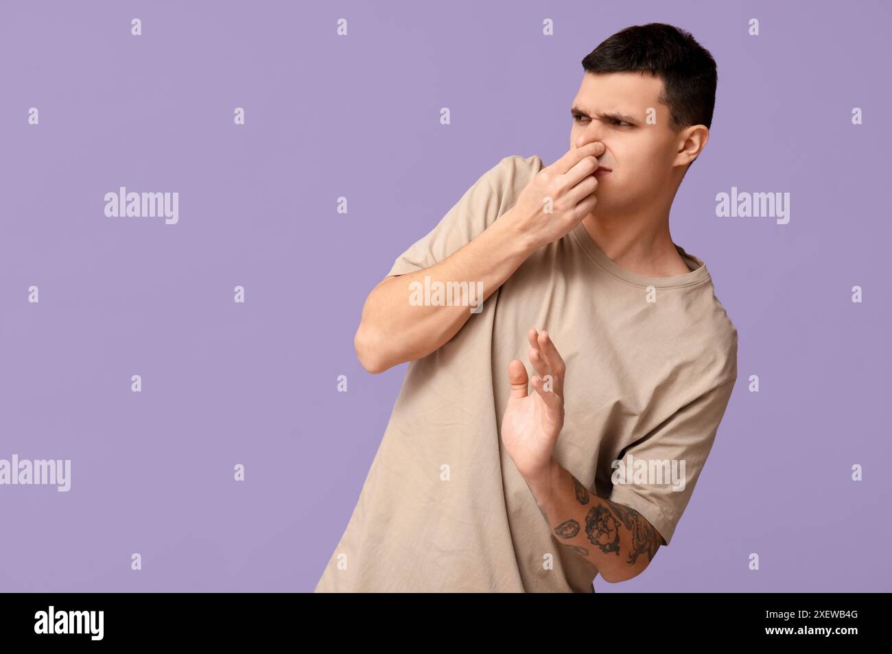 Handsome young man pinching nose because of bad smell on purple ...