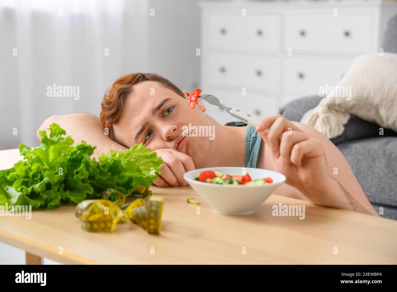 Young sad overweight man with bowl of healthy salad and measuring tape ...