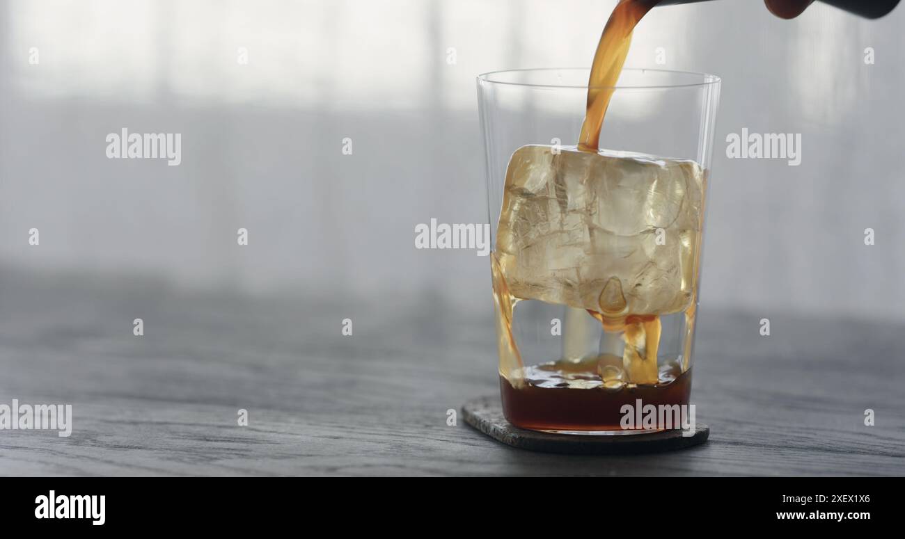coffee pour over ice cube in tumbler glass on black wood table, wide ...
