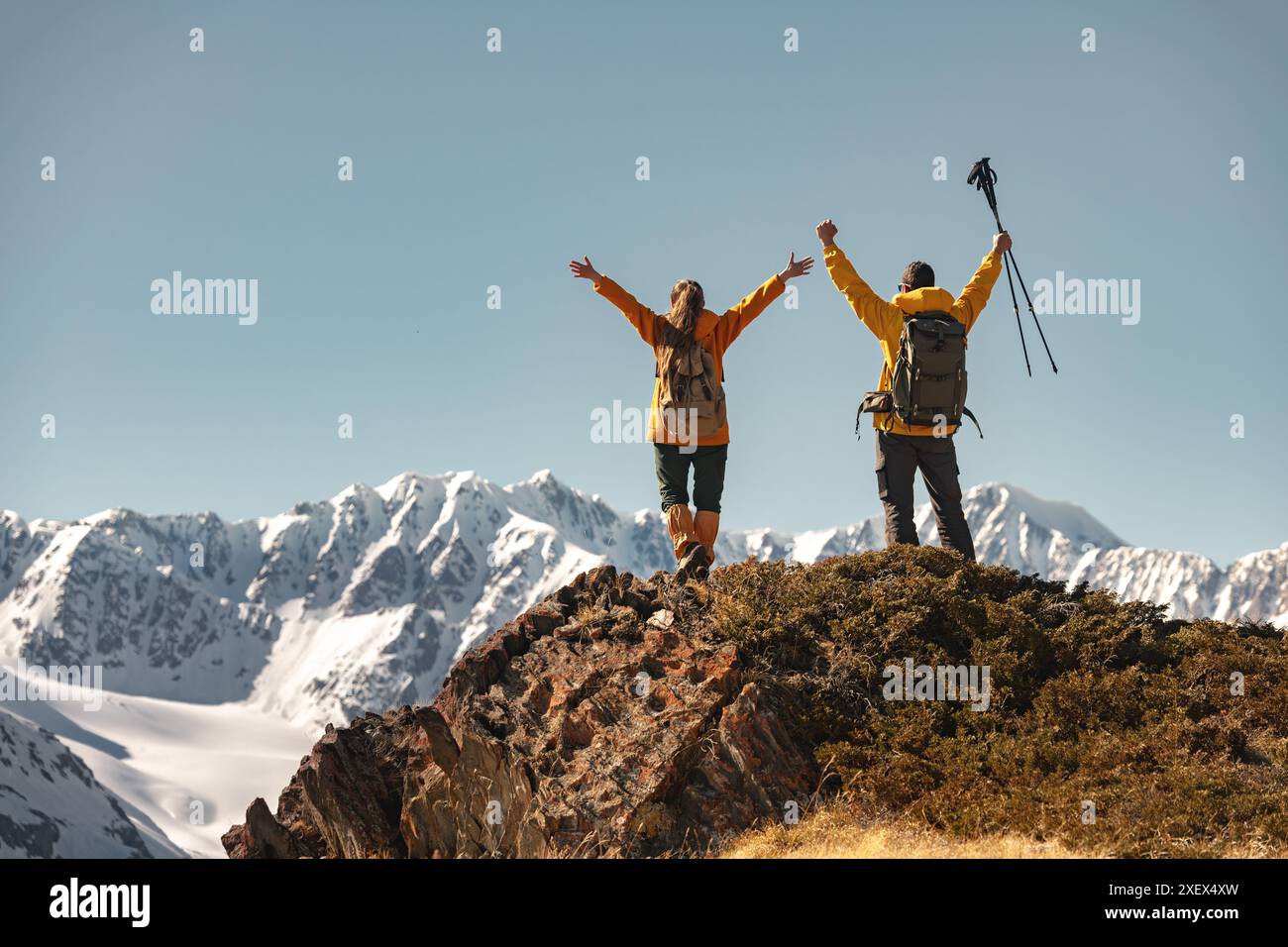 Two young happy successful hikers are standing in winner pose high in ...