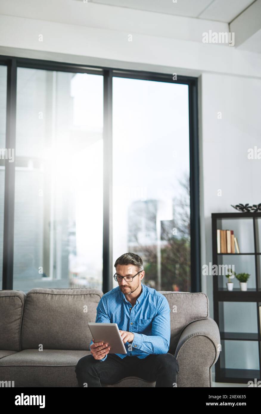 Man, tablet and typing in lounge, online and research of genre in home ...