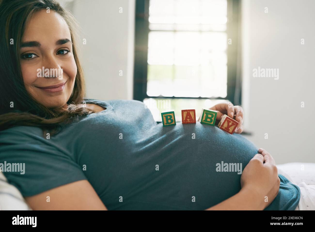 Portrait, smile and pregnant woman with blocks on stomach in home for ...