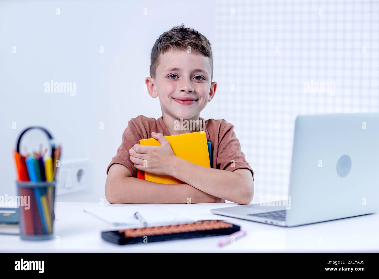 Smart schoolboy is ready to study at a neat table in a white interior ...