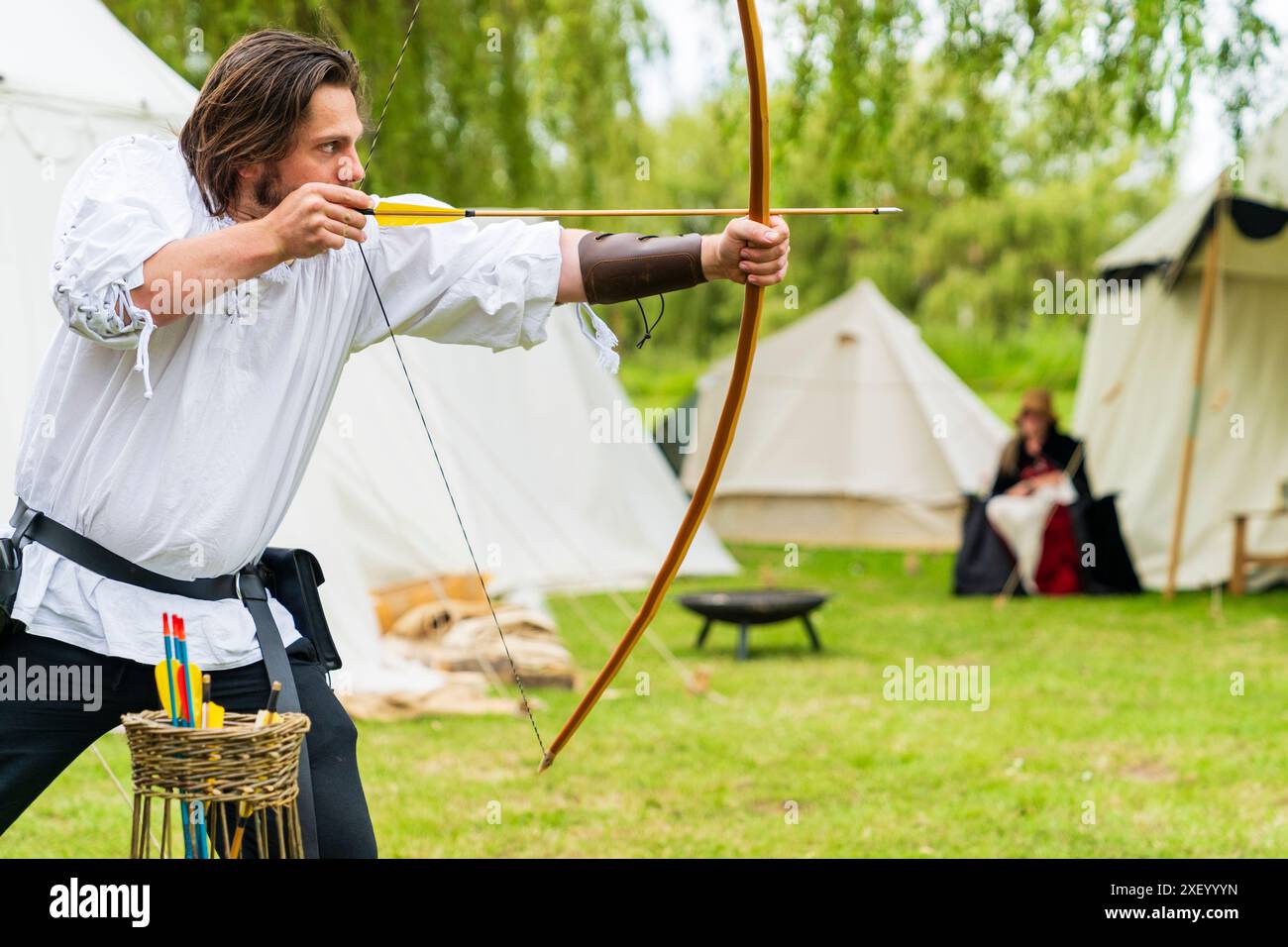 Close up side view of man in medieval costume taking aim with a bow and ...
