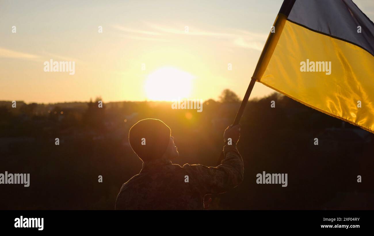 Male soldier stands with raised flag of Ukraine against background of ...