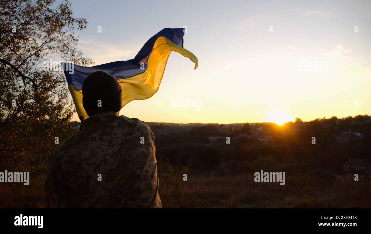 Young man in military uniform waving flag of Ukraine against beautiful ...
