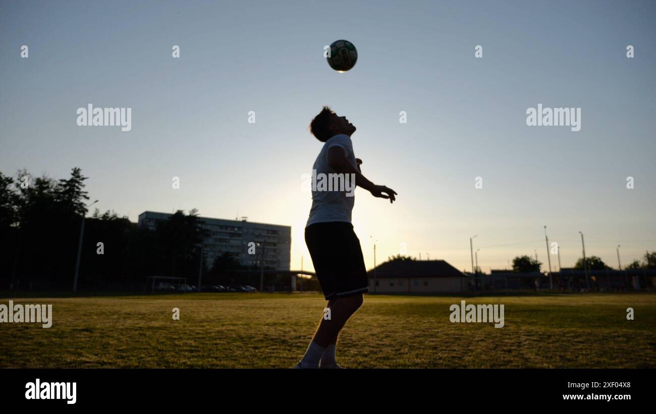 Professional footballer juggling soccer ball on stadium at sunset ...