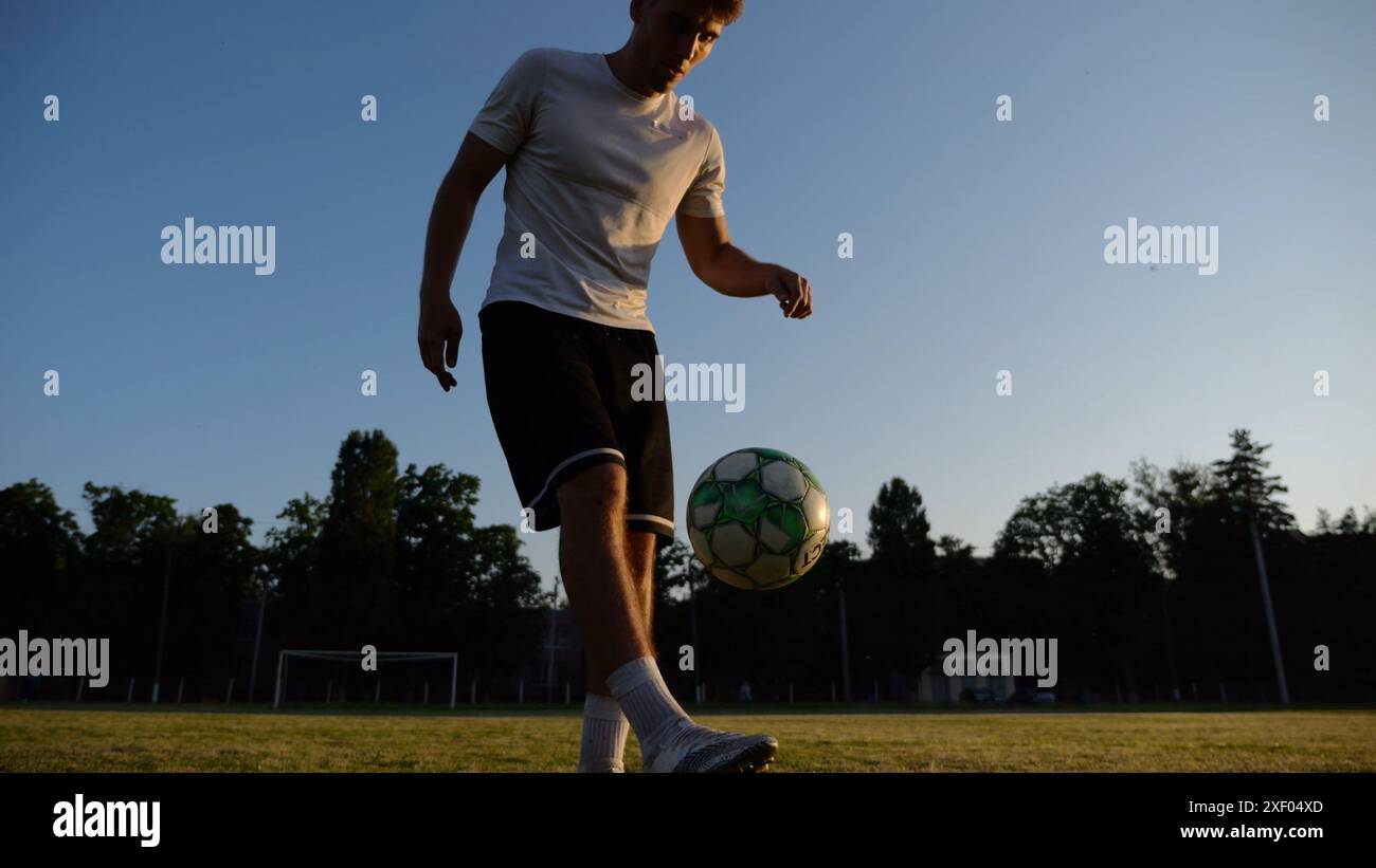 Professional footballer juggling soccer ball on stadium at sunset ...