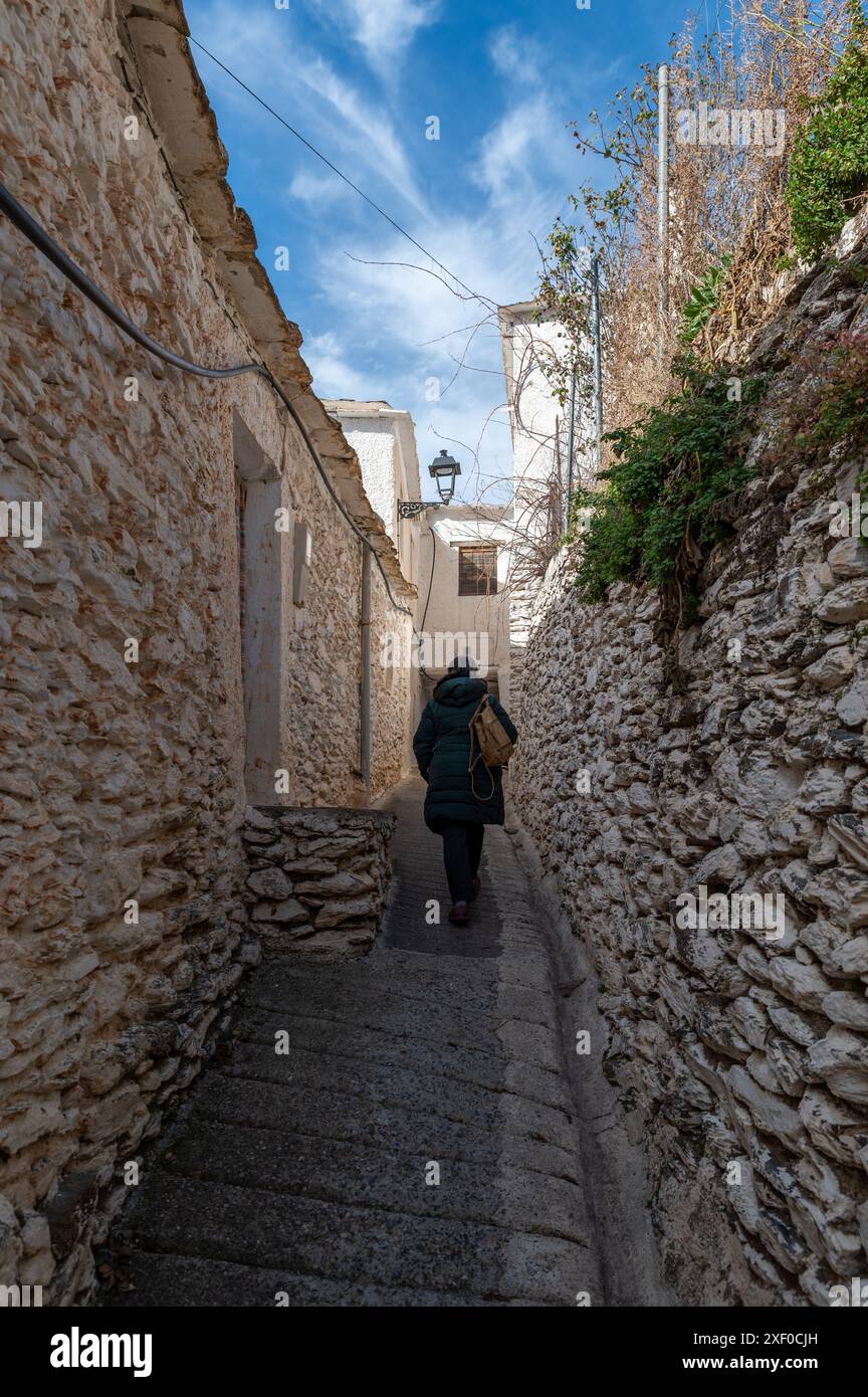 Woman seen from behind walking through the narrow streets of a town in ...