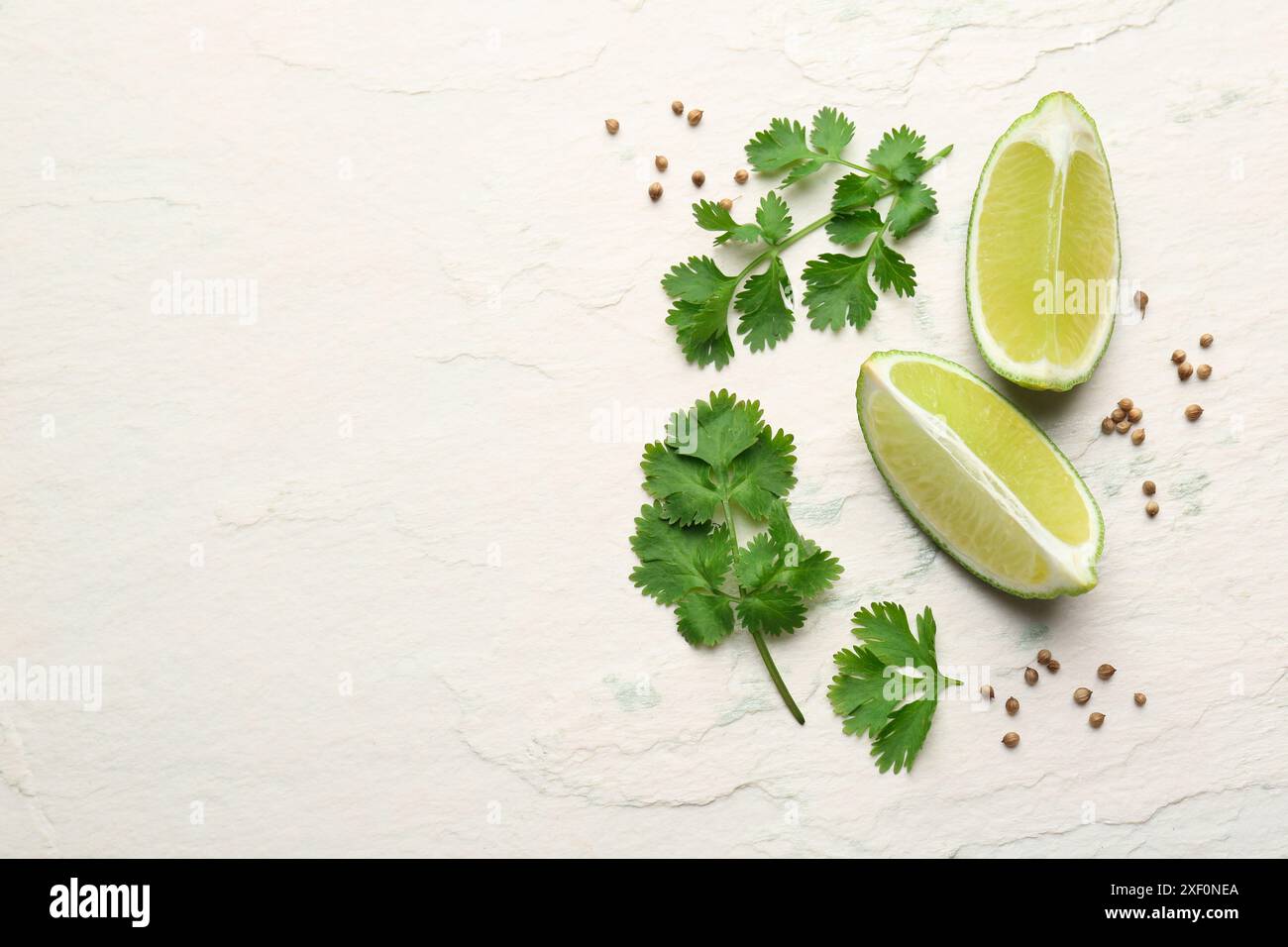 Fresh coriander leaves, dried seeds and lime wedges on light textured ...