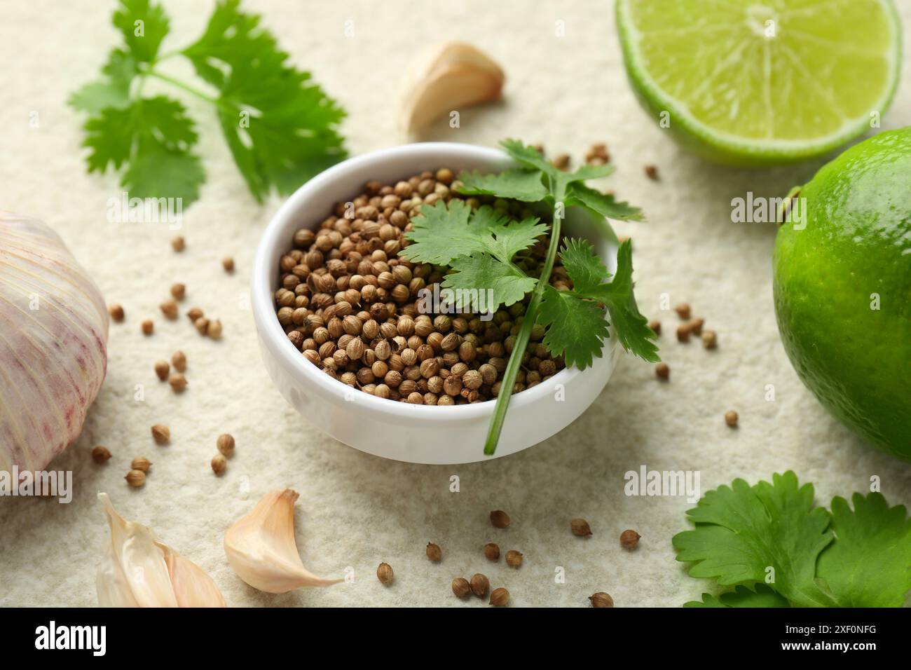 Fresh coriander leaves, dried seeds, garlic and limes on light textured ...