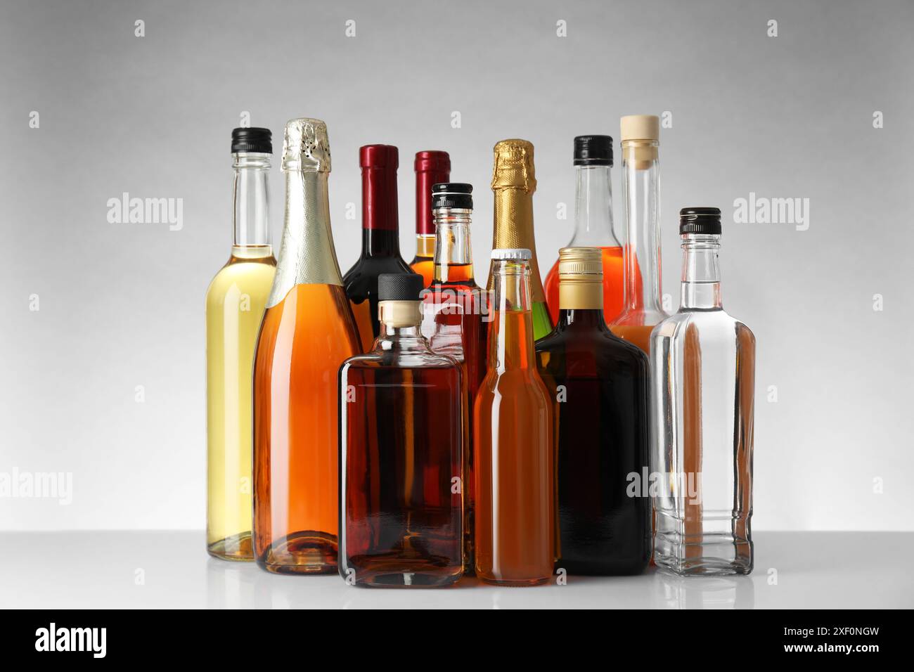 Bottles of different alcoholic drinks on white table against light ...