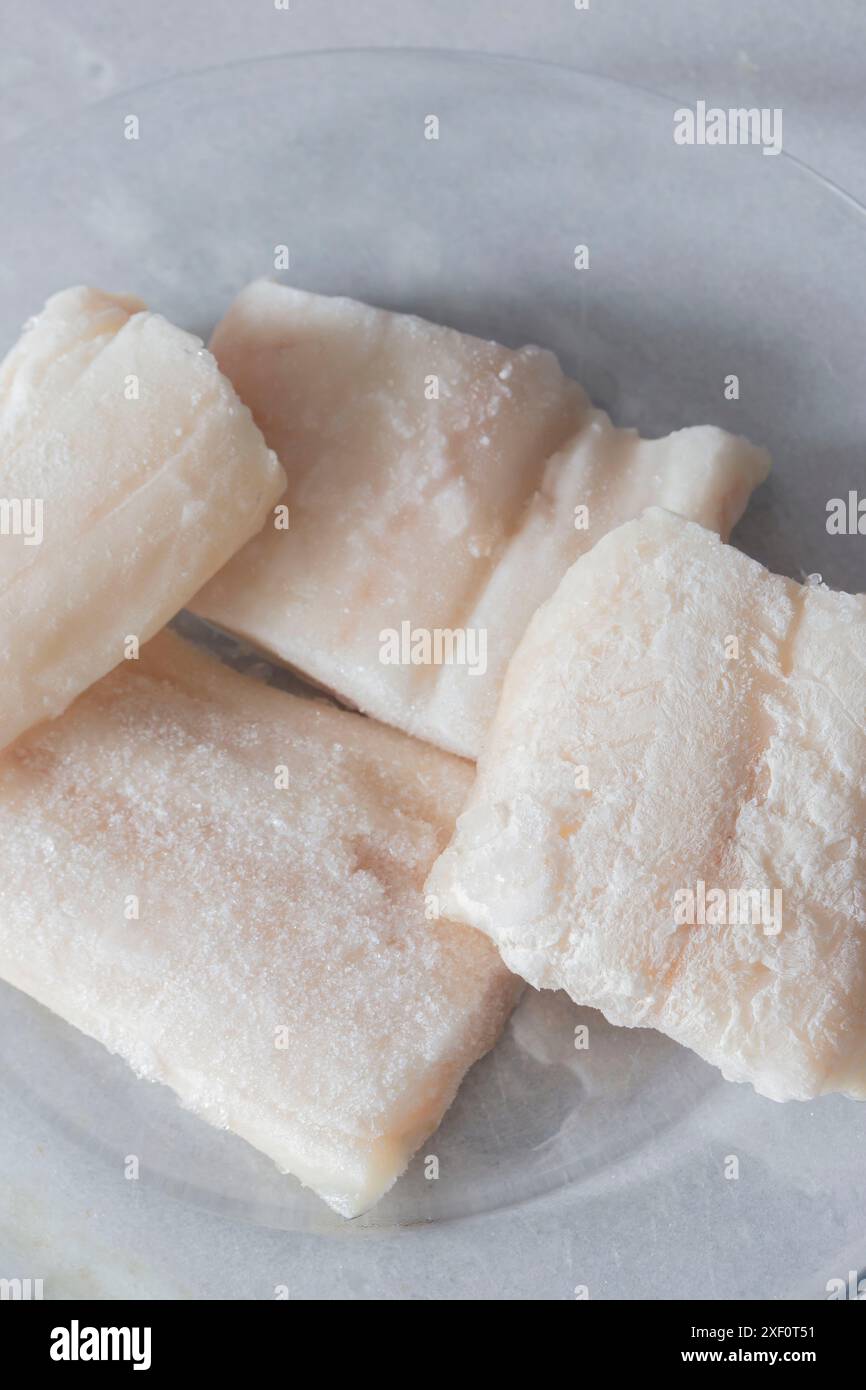 Frozen haddock fillets defrosting on a glass plate. On a light grey ...