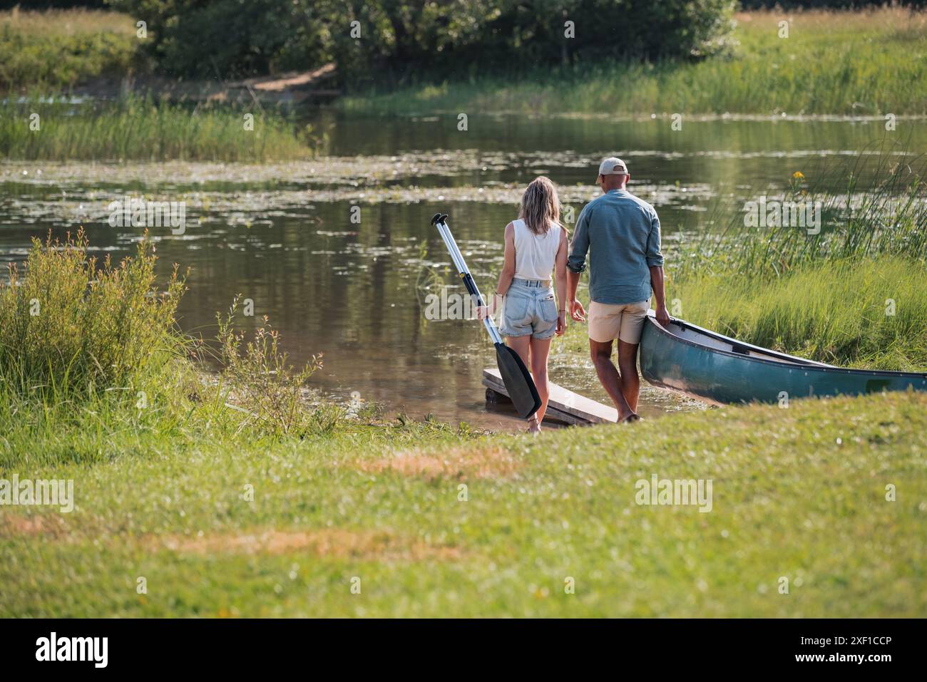 Young man and woman pulling a canoe into the water on the beautiful ...