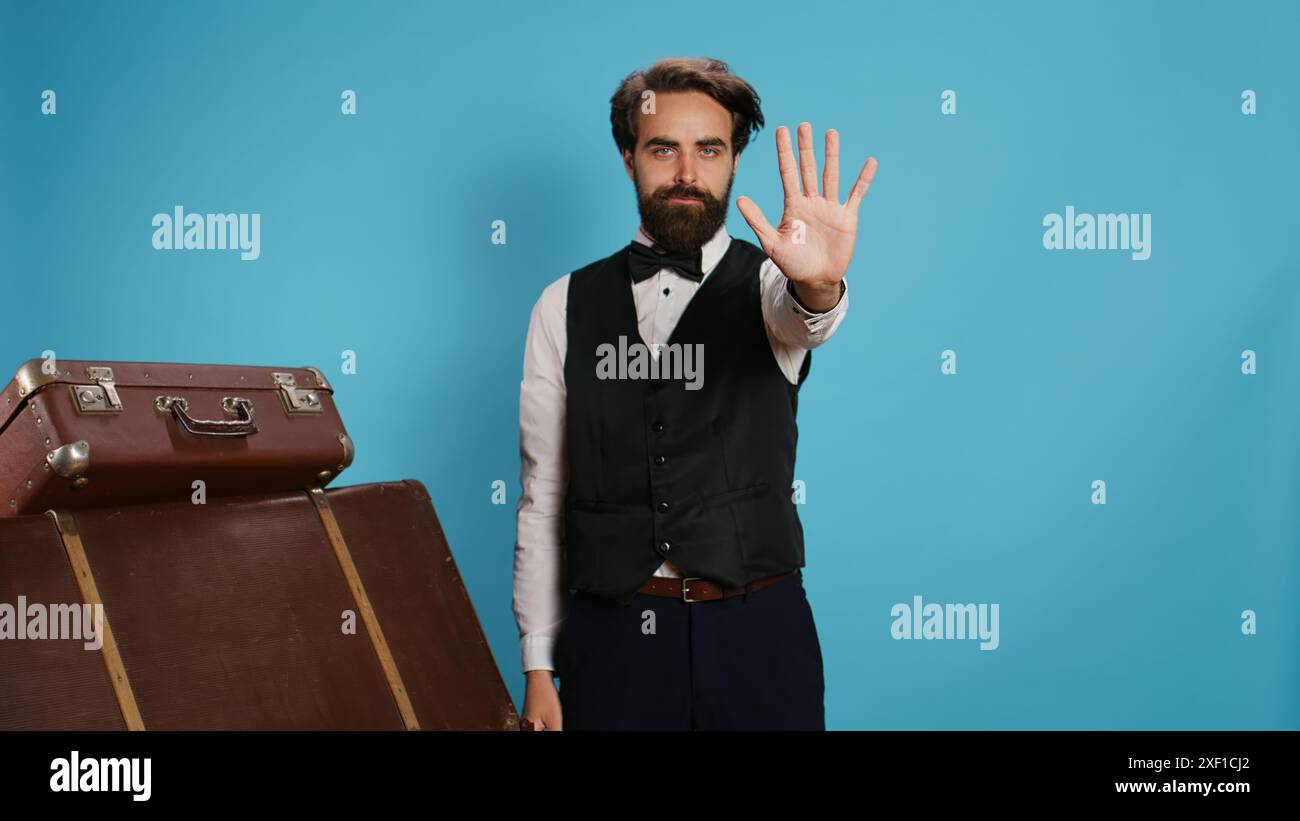 Bellboy raises hand to show stop sign against blue background, working ...