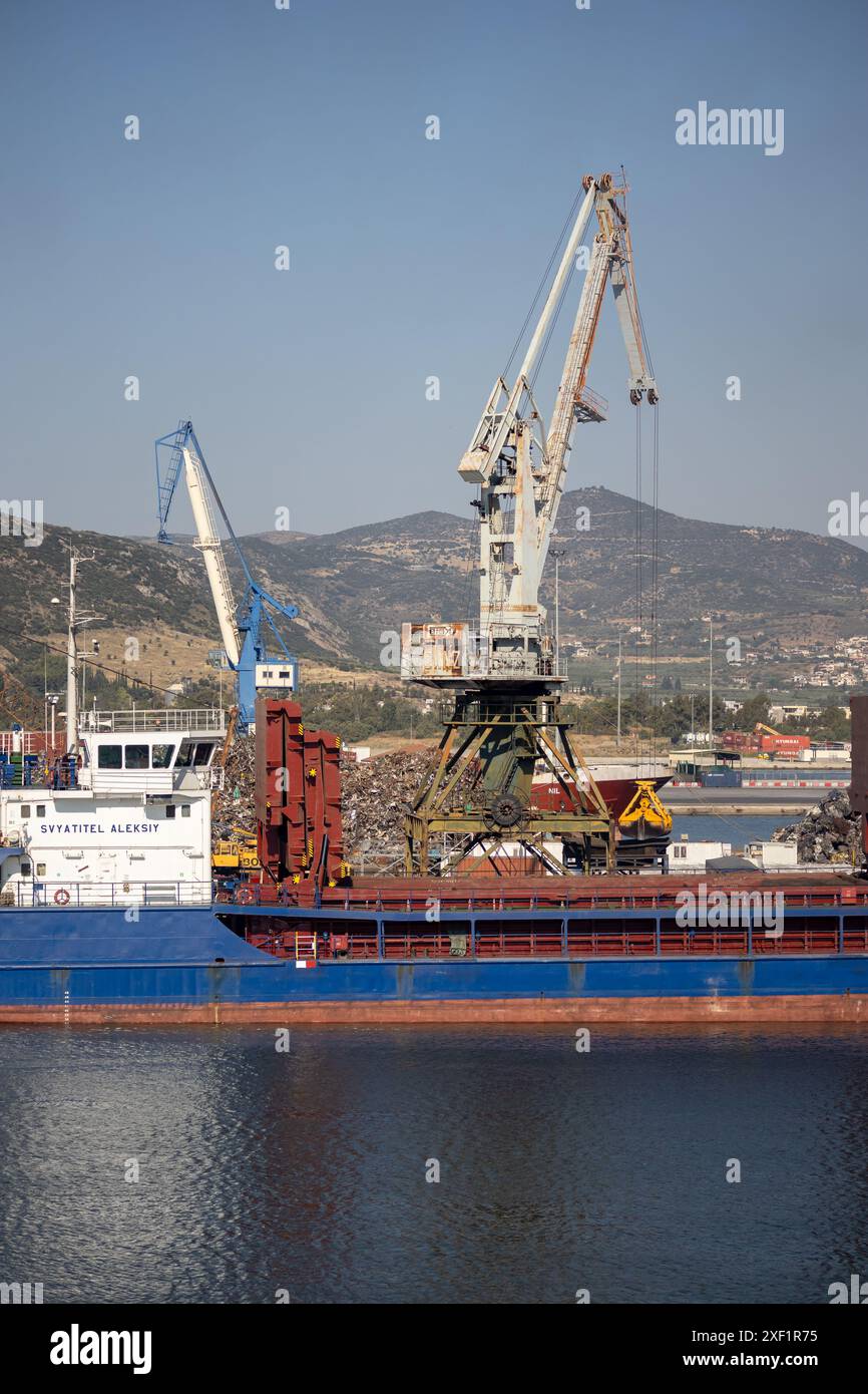 A large freight ship docked at a busy industrial port with cranes for ...