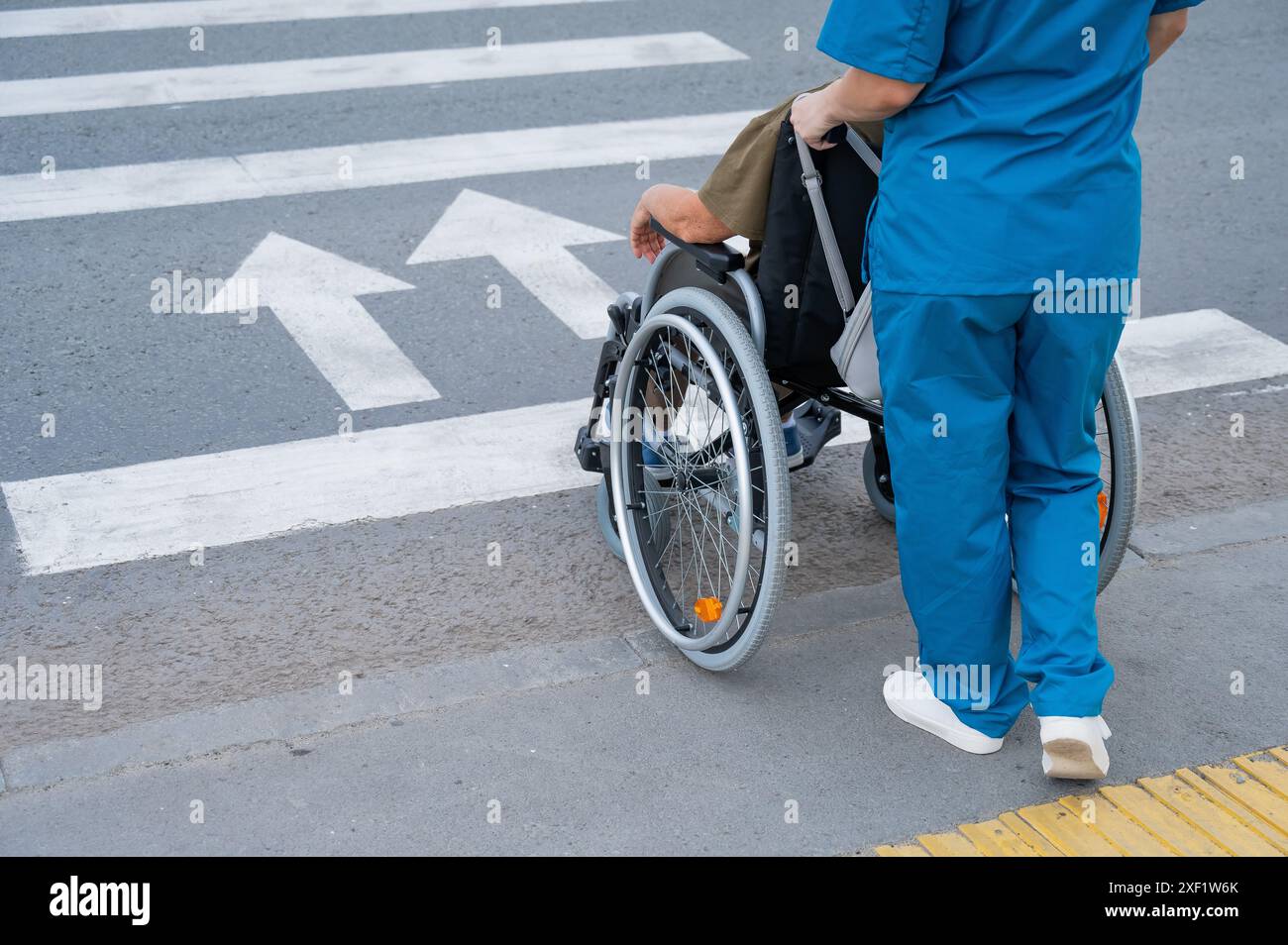 Rear view of a nurse helping an elderly woman in a wheelchair cross the ...