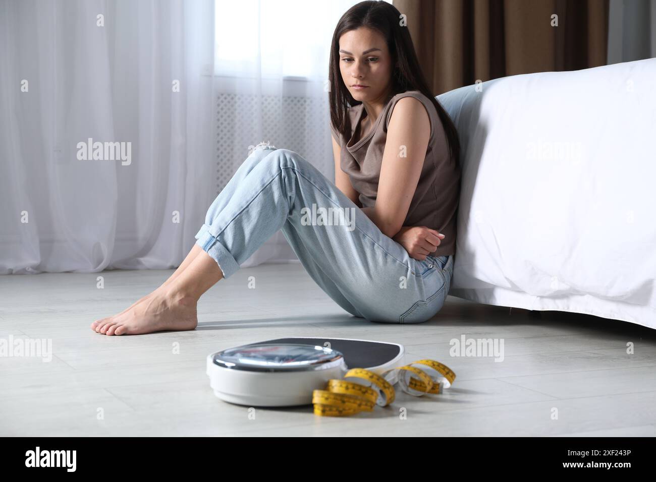 Eating disorder. Sad woman sitting near scale and measuring tape on ...