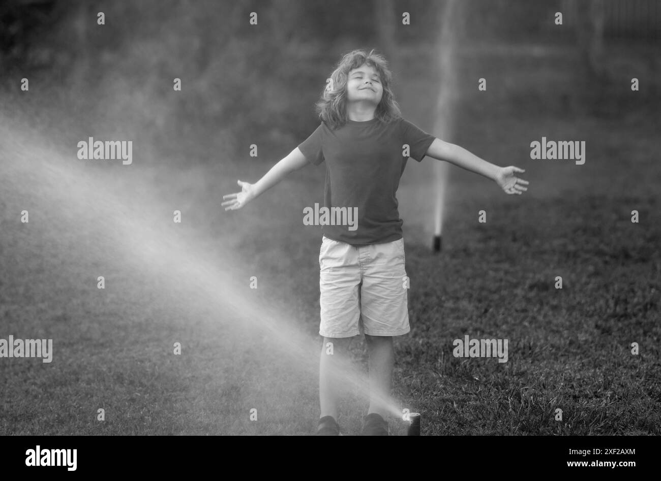 Child play in summer garden. Grass watering. Automatic sprinkler irrigation system in a green ...