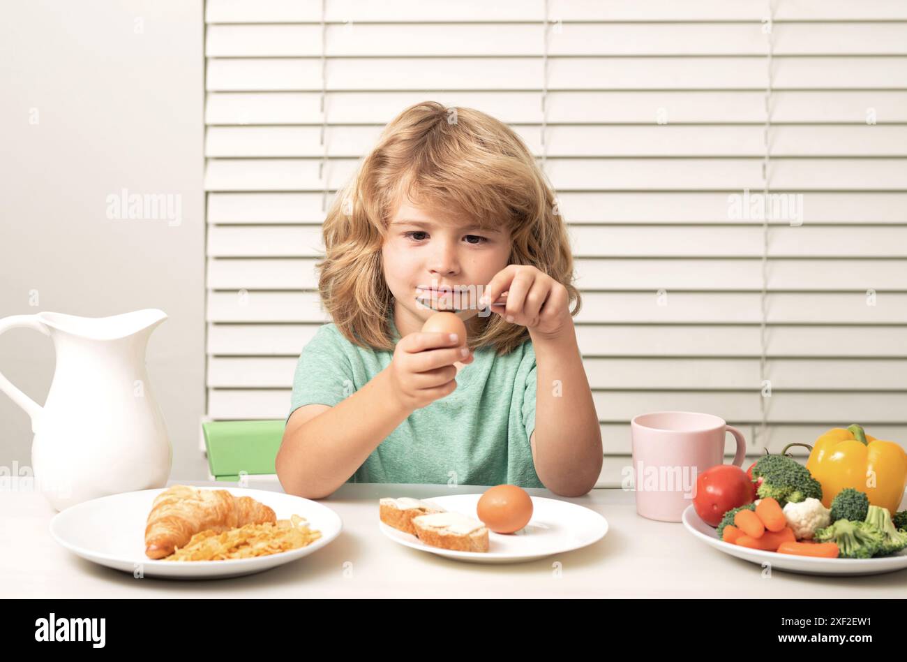 Child eating egg. Child in the kitchen at the table eating vegetable ...