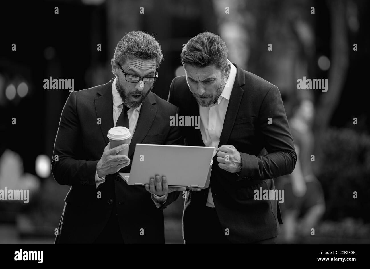 Two handsome young businessmen in classic suits using laptop. Business ...