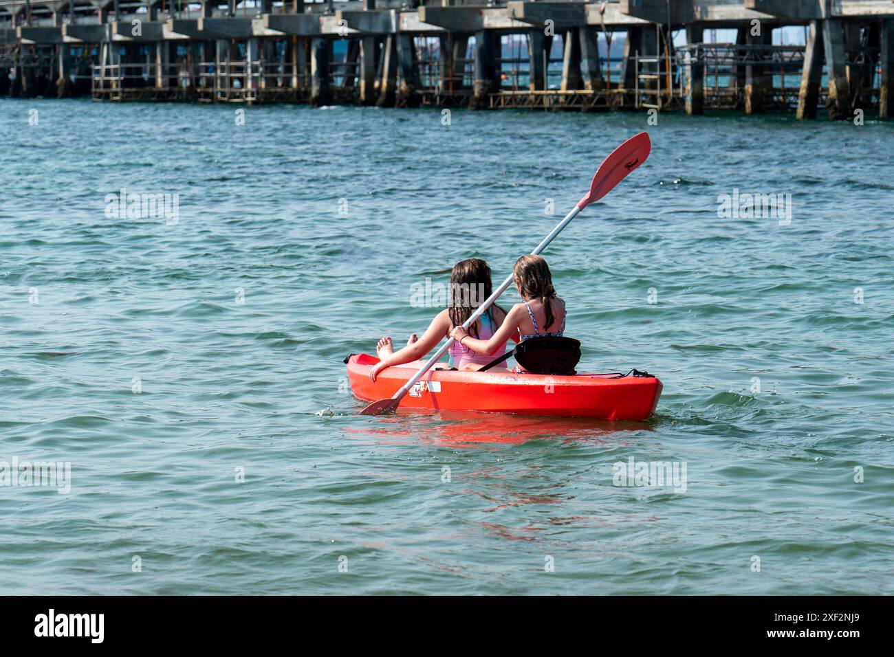 Two girls from behind paddling a red kayak ocean blue Stock Photo - Alamy