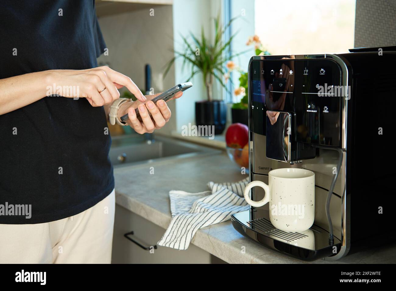 Person uses smartphone app to operate coffee machine. Woman preparing ...