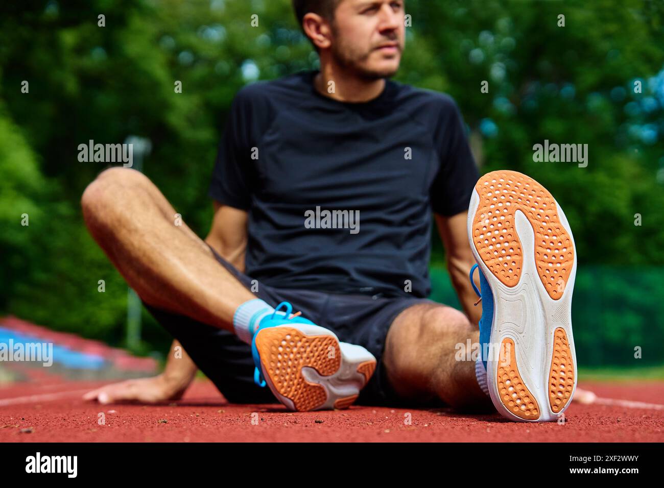 Male athlete wearing running shoes sits on stadium track, resting and ...