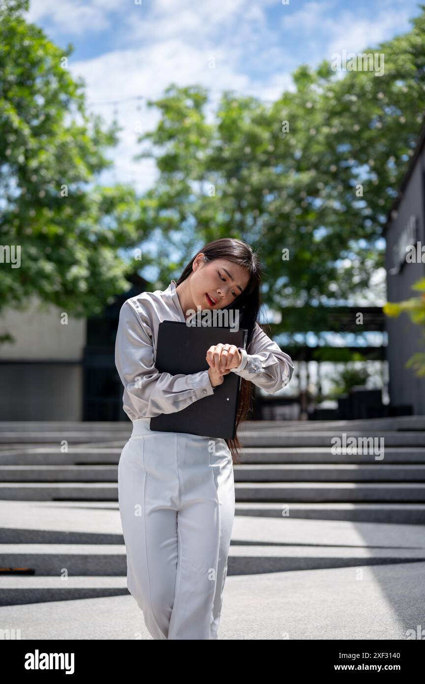 A busy, frustrated Asian businesswoman with a file folder is talking on ...