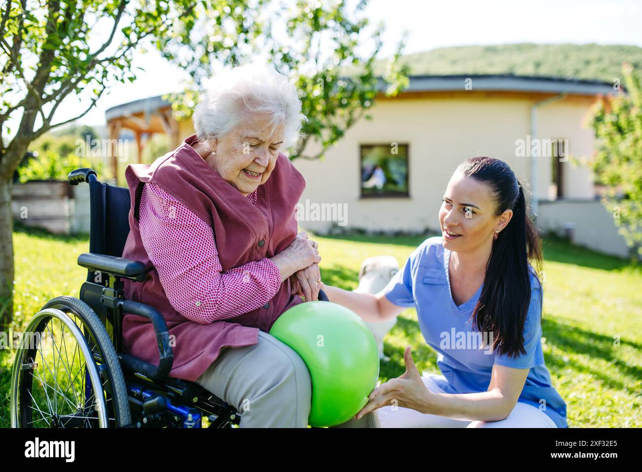 Female caregiver doing motorized exercises with senior woman in ...