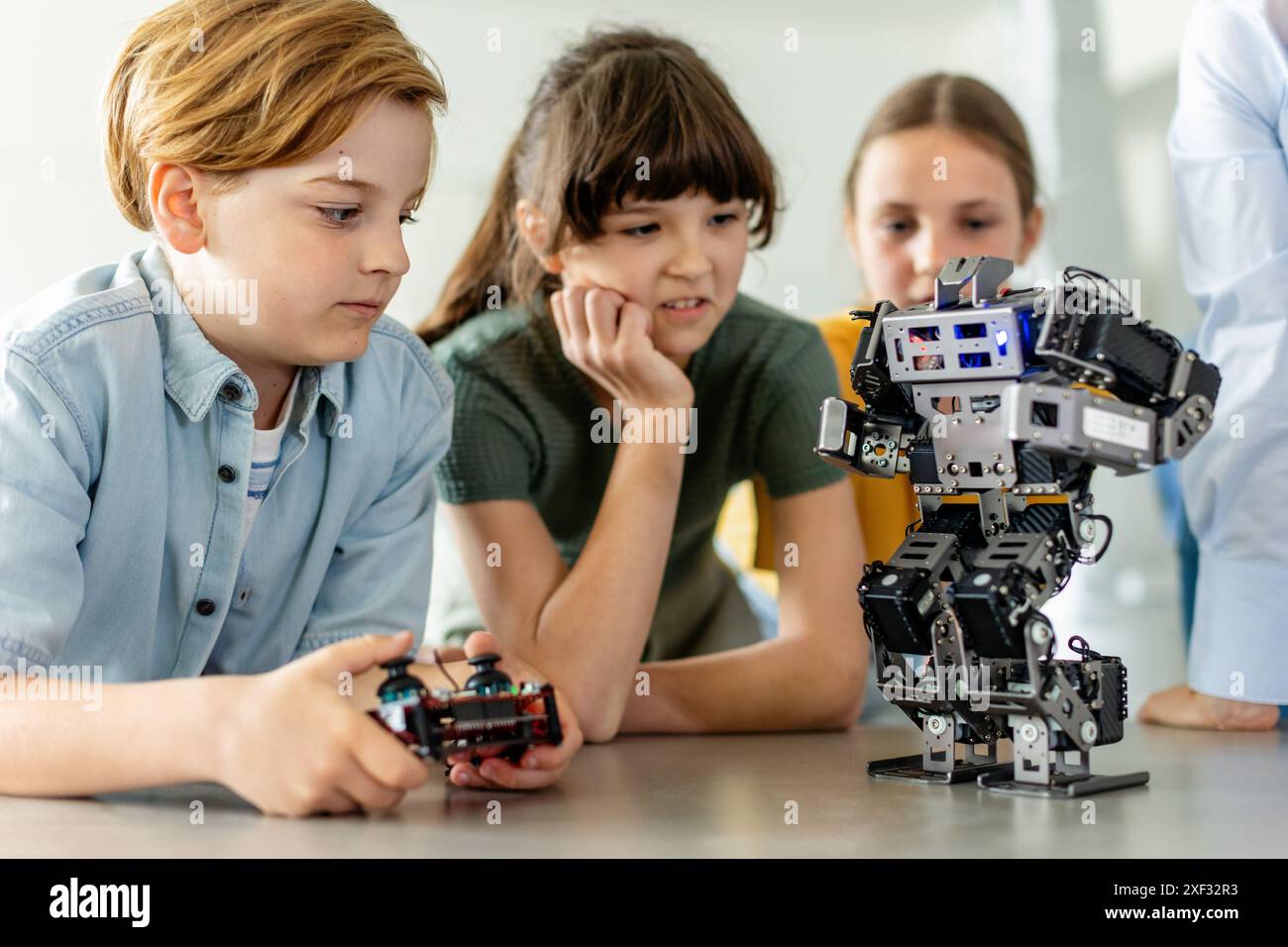 Children looking at small robot, learning robotics in elementary school ...