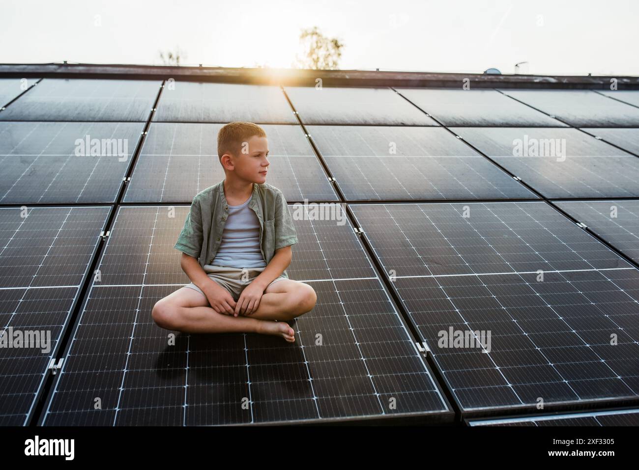 Cute boy sitting on roof with solar panels, looking at surrounding ...
