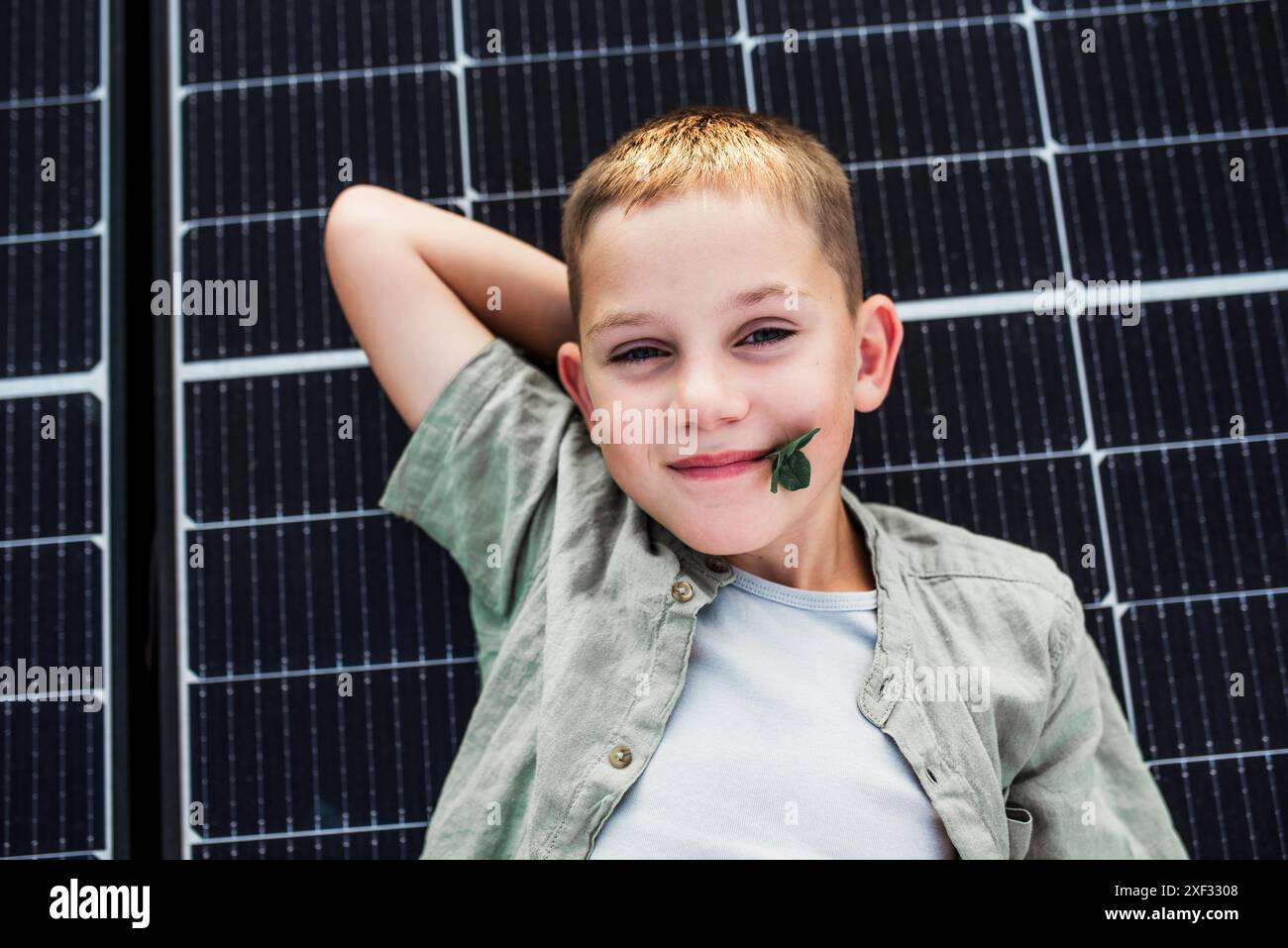 Top view of boy lying on roof with solar panels, looking at camera ...