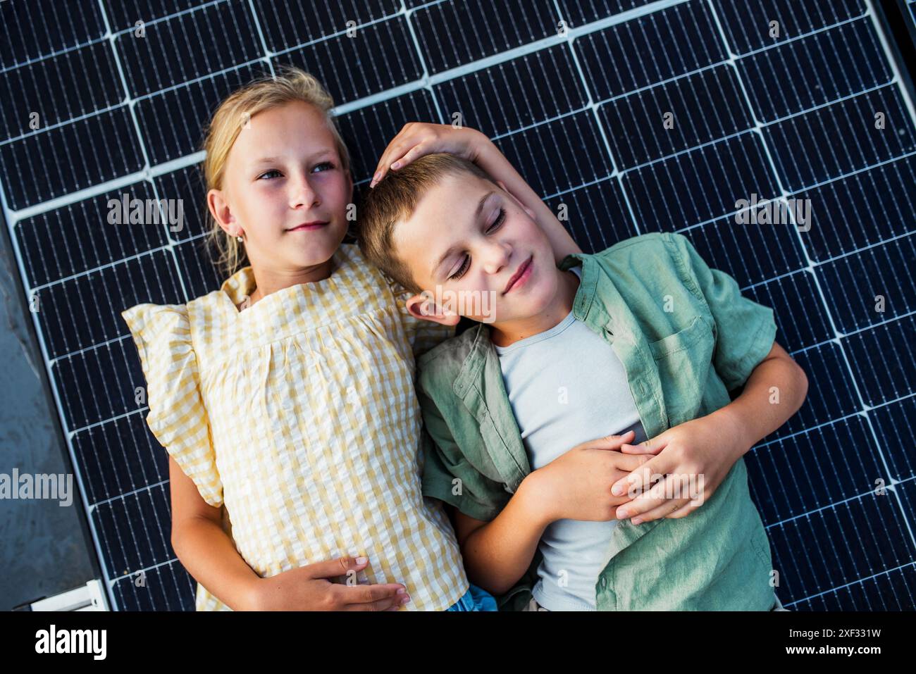 Top view of two young siblings lying on roof with solar panels. Rooftop ...