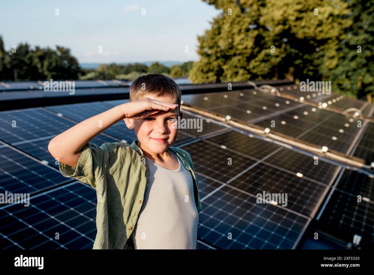 Cute boy on roof with solar panels, hand shielding eyes from summer sun ...