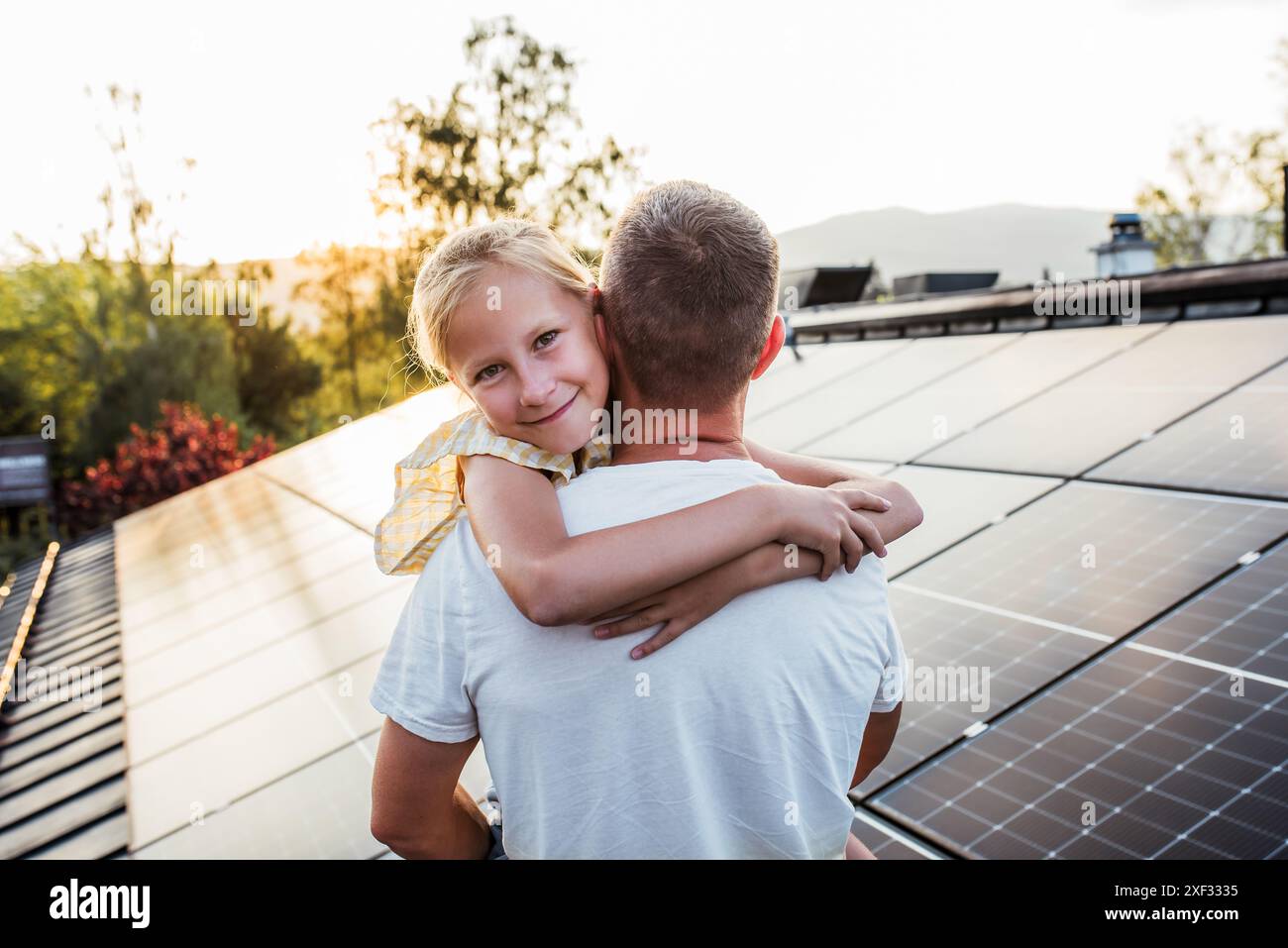 Dad holding girl, standing in front of roof with solar panels during ...