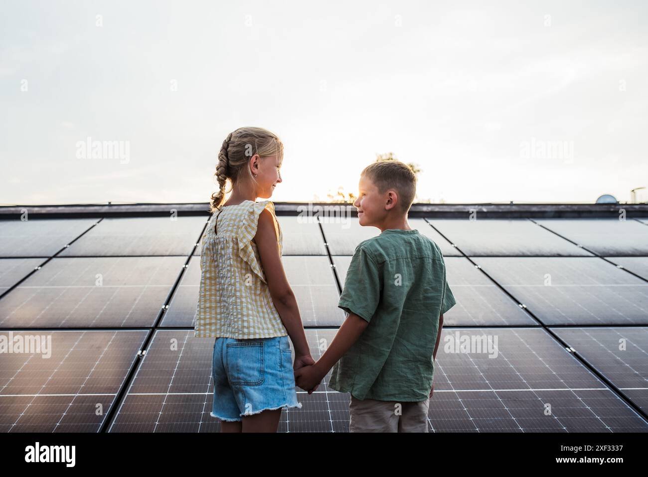 Two young siblings on roof with solar panels, looking at each other ...