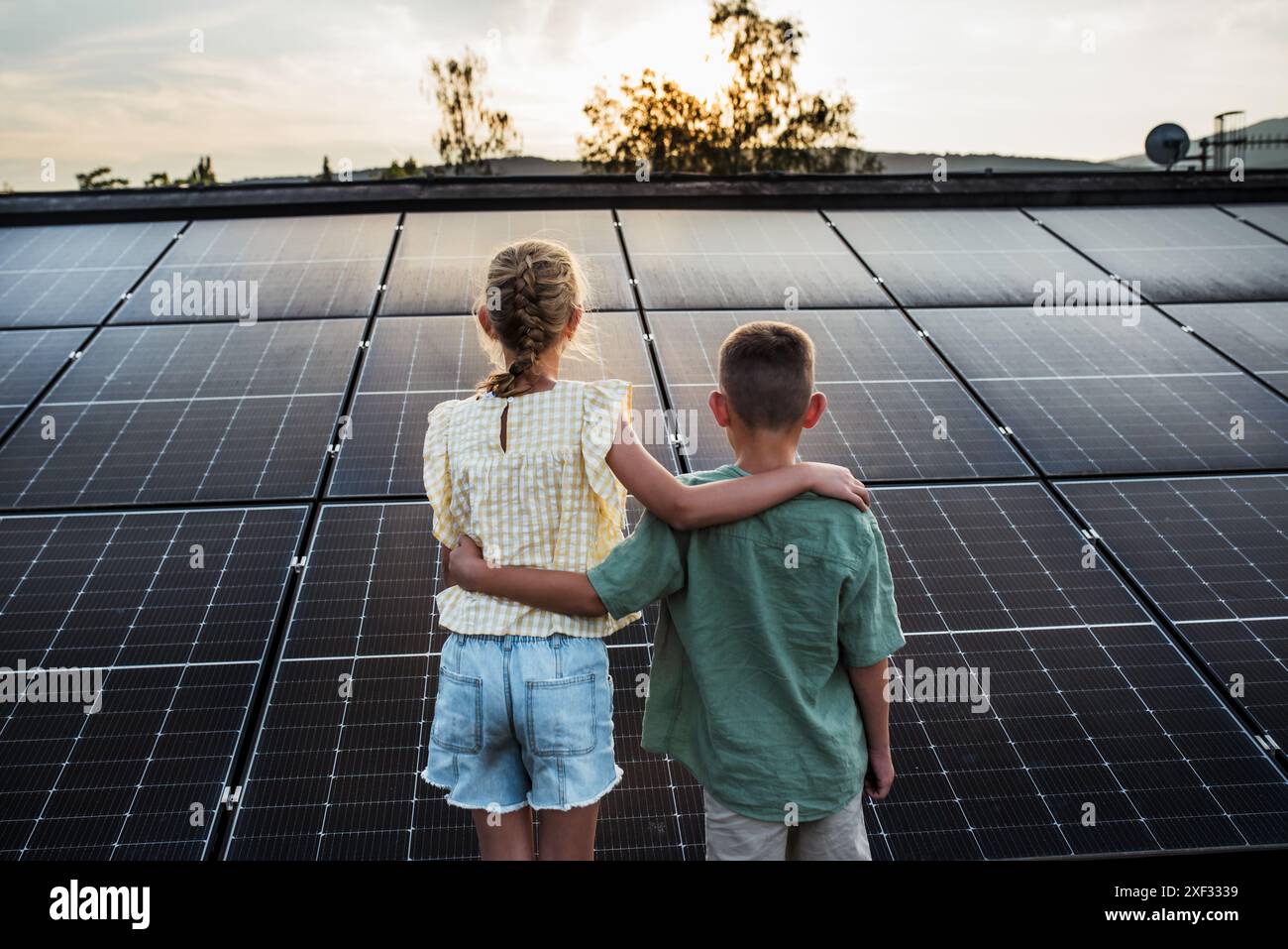 Two young siblings on roof with solar panels, holding each other ...