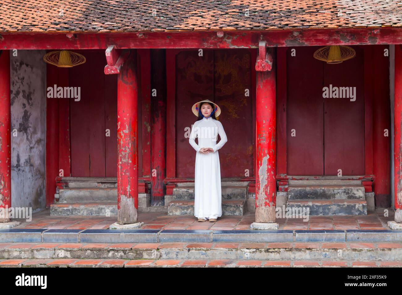 Pretty Vietnamese young woman wearing traditional Ao Dai tunic and conical hat at Temple of ...