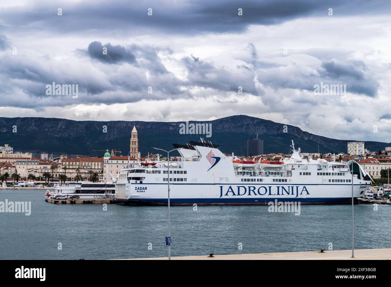 Large Jadrolinija ferry docked under a cloudy sky, with other ships in the background, Split ...