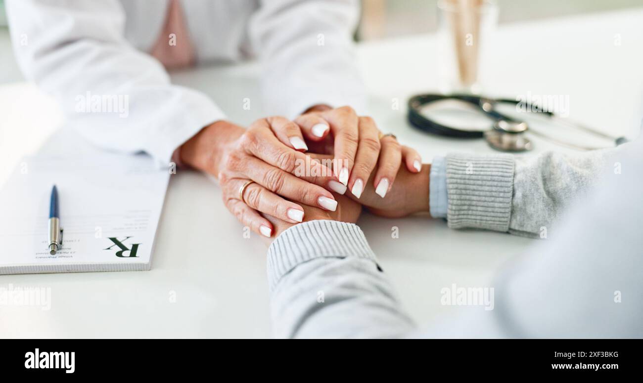 Doctor, patient and holding hands on desk in consultation room with ...